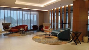 Uma sala de estar moderna com janelas amplas, um sofá vermelho, uma poltrona azul e uma pequena mesa de centro.