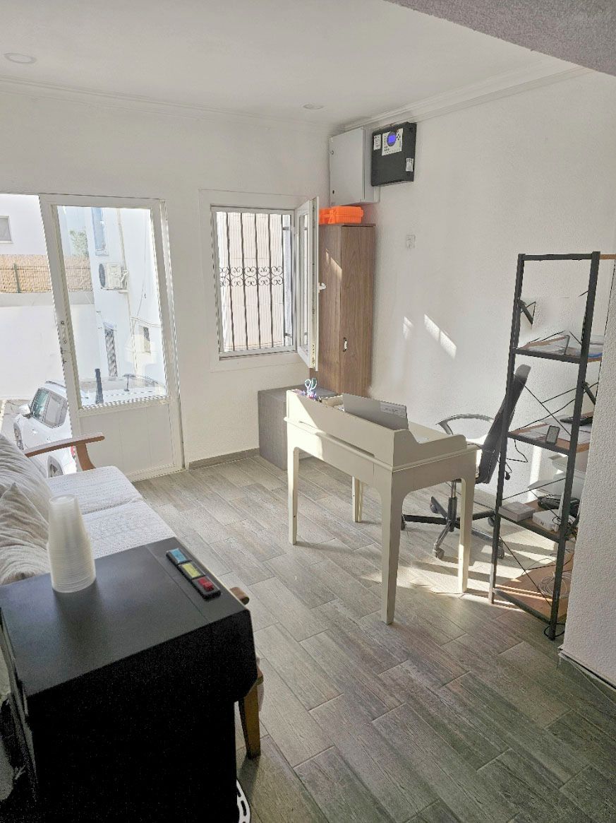 Quarto com cama, escrivaninha, cadeira, janela com grades e prateleira com objetos.