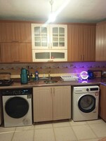 Cozinha compacta com armários de madeira, máquina de lavar, secadora, cafeteira e chaleira.