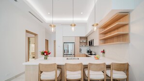 Cozinha moderna com ilha central, cadeiras de madeira, luminárias pendentes e prateleiras embutidas.