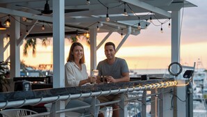 Um casal sentado à mesa com vista para o porto e o pôr do sol.