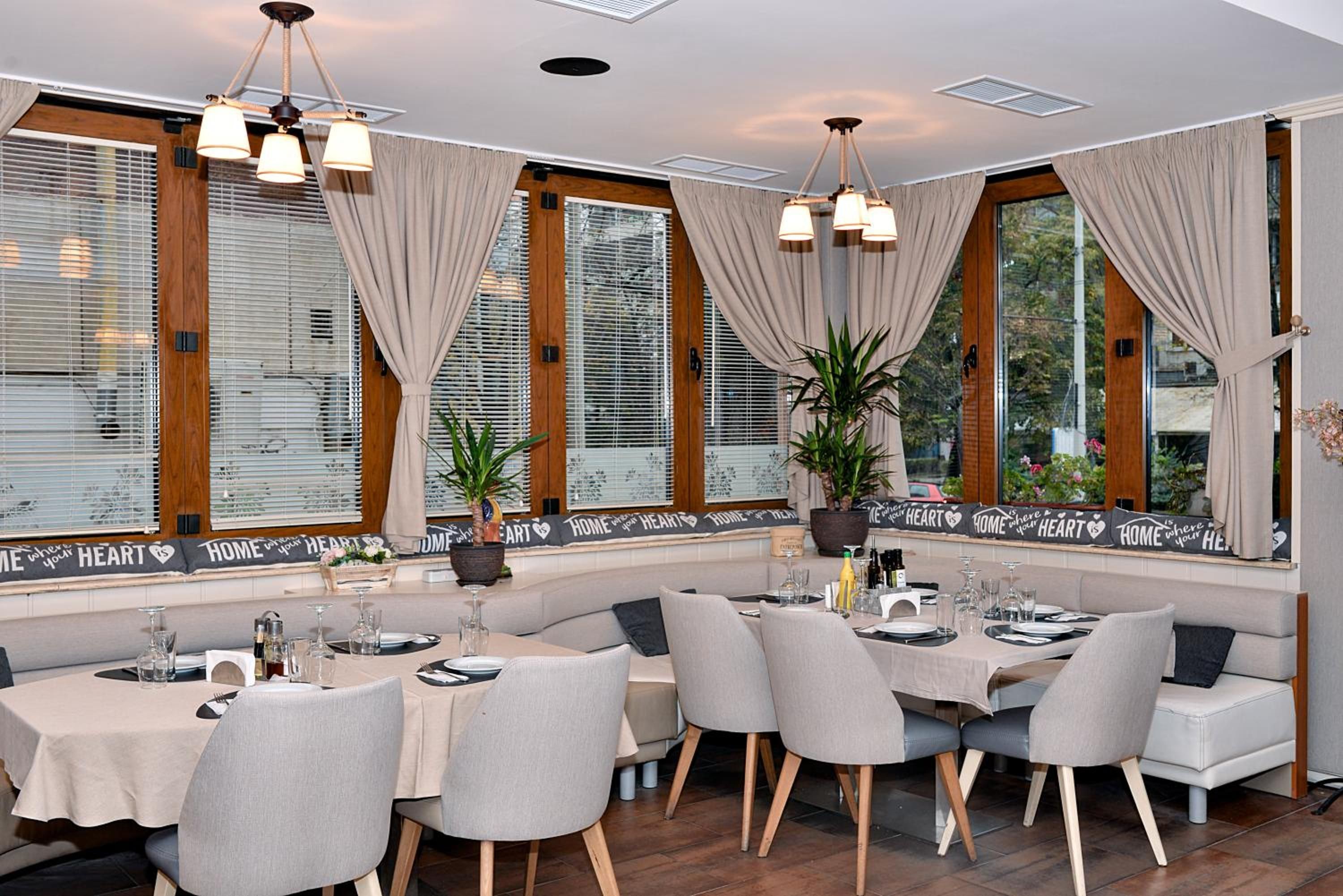 Uma área de jantar com mesas para quatro pessoas, grandes janelas com cortinas e vista para o exterior.