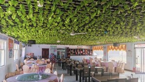 Um restaurante com mesas e cadeiras, área de bar e teto coberto por folhagem verde.