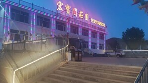 Um edifício com uma escadaria que leva a uma entrada bem iluminada, um veículo estacionado na frente e uma placa com caracteres chineses.