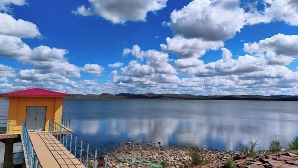 Um lago tranquilo sob um céu claro, com um pequeno edifício de telhado vermelho.