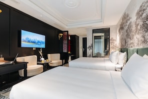Quarto de hotel com duas camas, uma escrivaninha com um laptop, uma televisão e uma janela grande.