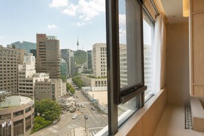 Vista da janela de um quarto de hotel com vista para a paisagem urbana, com edifícios modernos e uma torre imponente.