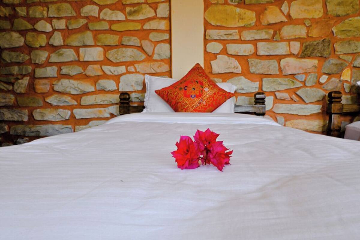 Cama com roupa de cama branca, um travesseiro decorativo vermelho e um buquê de flores vermelhas.
