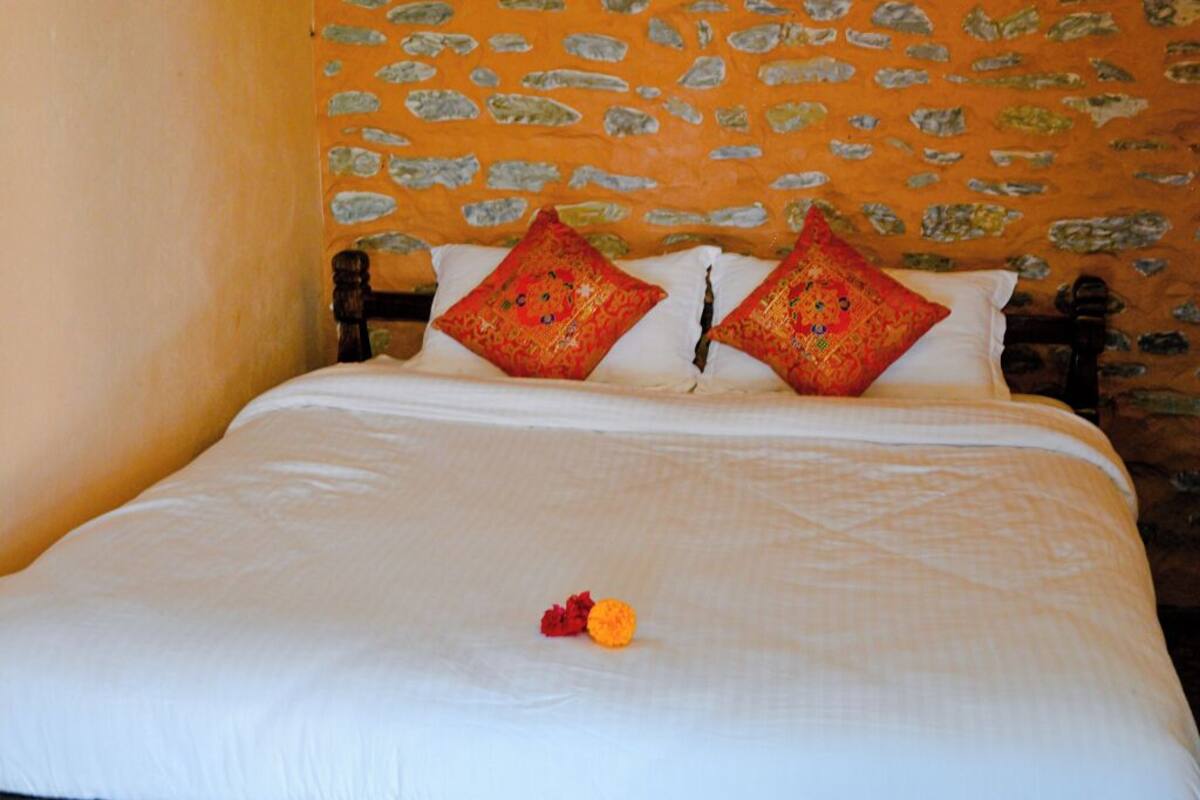 Uma cama com roupa de cama branca, duas almofadas vermelhas e um pequeno objeto laranja sobre a cama.