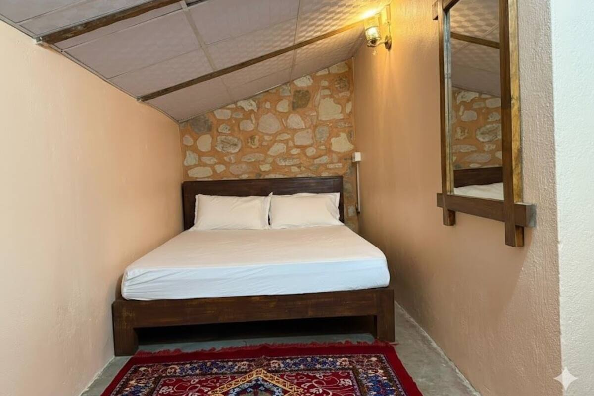 Quarto com cama de madeira, parede de pedra e tapete vermelho estampado.