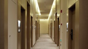Corredor de hotel com várias portas, cada uma com uma luz acima e uma pequena placa na parede.