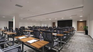 Uma sala de conferência com fileiras de mesas e cadeiras, um quadro branco e uma tela de projeção.