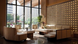 Um lobby moderno com grandes janelas, área de estar com sofás e poltronas, e parede decorativa com padrão de grade.