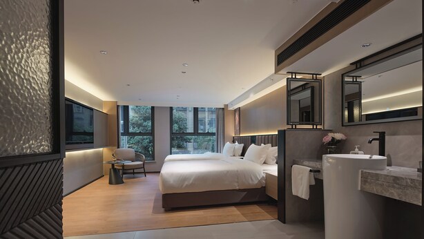 Quarto moderno com cama grande, mesas de cabeceira, toucador com espelho e janela com vista para o exterior.