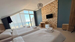 Quarto de hotel com duas camas, televisão, escrivaninha e vista para o mar.