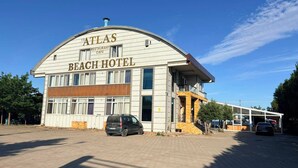 Um edifício de dois andares com um telhado curvo, com a placa 'The Atlas Beach Hotel'.