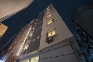 Um edifício de vários andares com janelas iluminadas, aparelhos de ar condicionado e uma entrada visível.