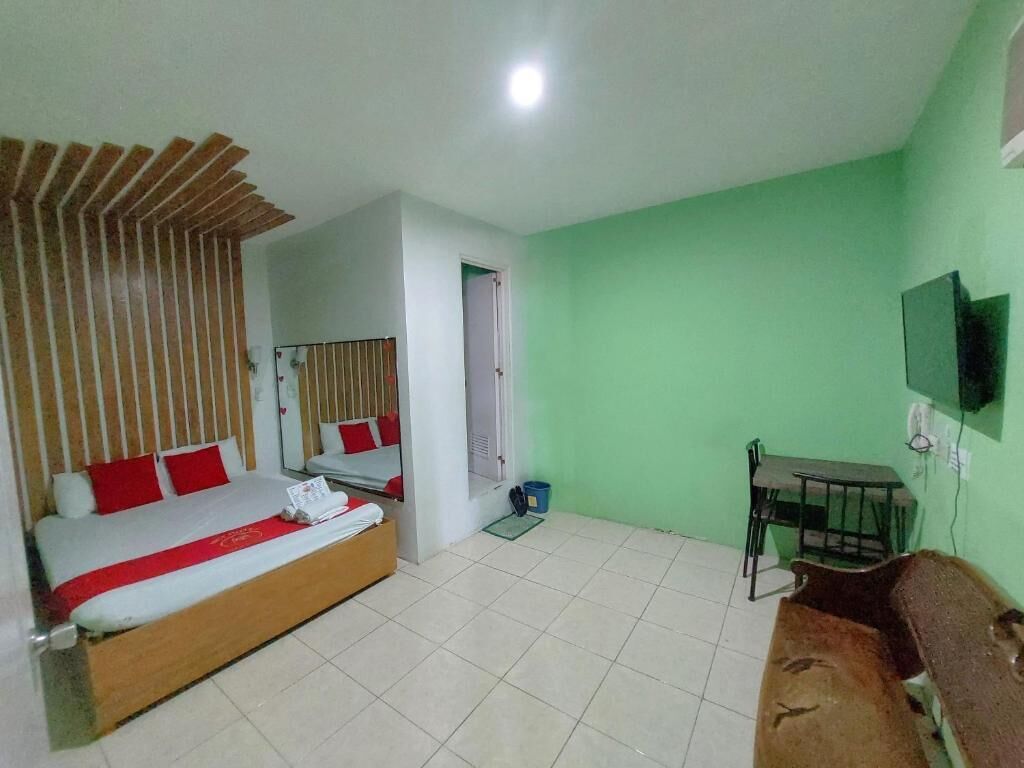 Quarto de hotel com cama, escrivaninha, cadeira, televisão e porta.