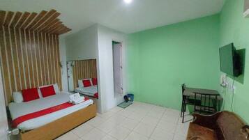 Quarto de hotel com cama, escrivaninha, cadeira, televisão e porta.