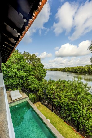 Piscina com vista para um lago e árvores, área coberta com guarda-corpo e céu claro.