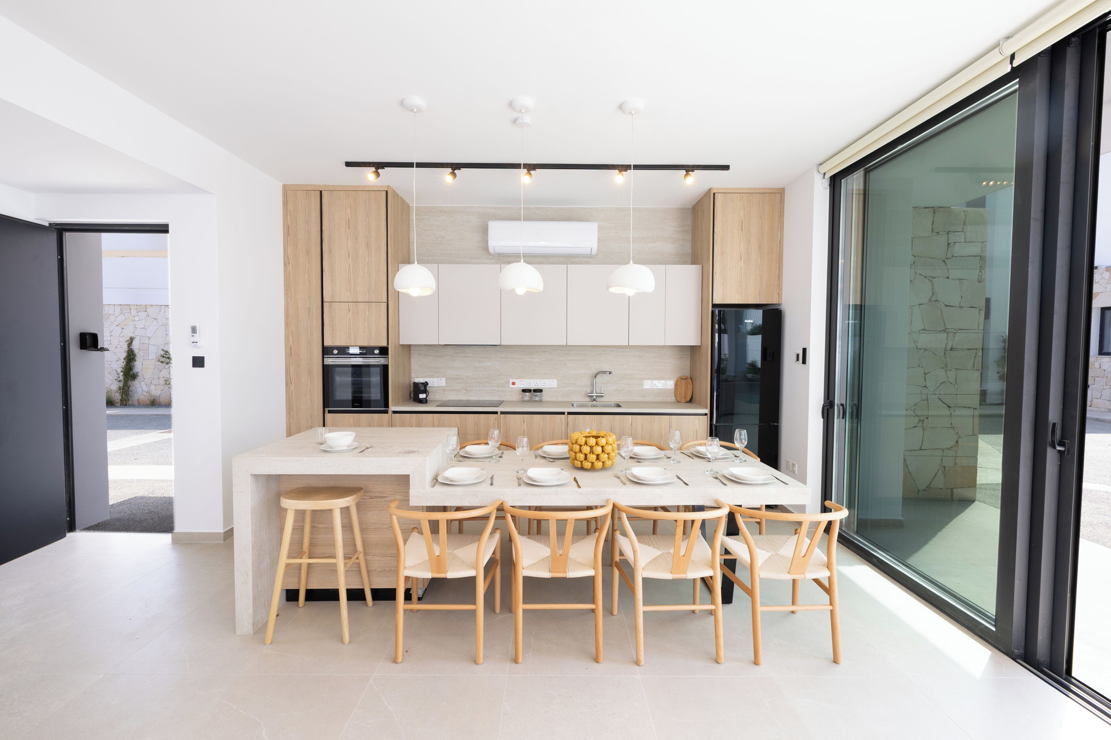 Cozinha moderna com ilha central, luminárias pendentes e área de refeições com cadeiras e mesa para seis pessoas.