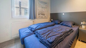 Quarto com duas camas, janela com cortinas, radiador e um quadro na parede.