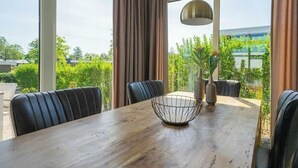 Uma mesa de jantar com cadeiras, um lustre pendurado e vista para o verde lá fora.