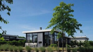 Um edifício moderno com fachada de vidro, rodeado por vegetação e um espaço pavimentado.
