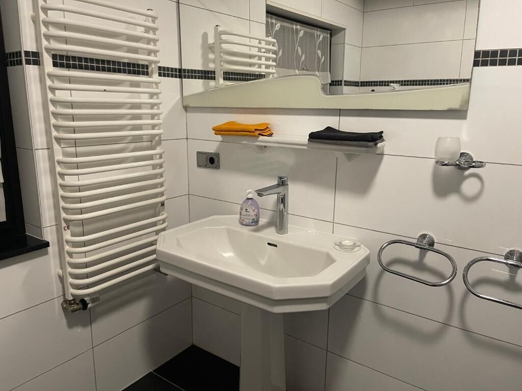 Uma casa de banho com uma pia branca, um espelho, um porta-toalhas e um aquecedor de toalhas.