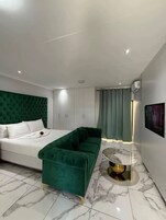 Quarto moderno com cama, sofá verde e piso de mármore.