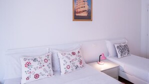 Quarto com duas camas, almofadas florais, mesa de cabeceira com abajur e um quadro na parede.
