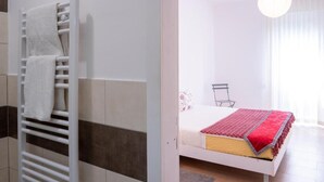 Quarto com uma cama, um radiador branco e uma janela com cortinas.
