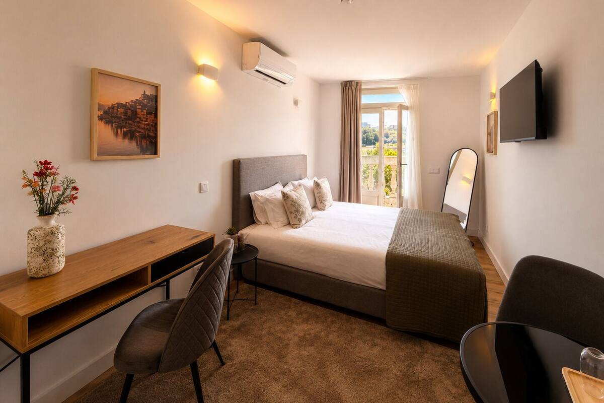 Quarto de hotel com cama, escrivaninha, cadeira, televisão e um quadro.
