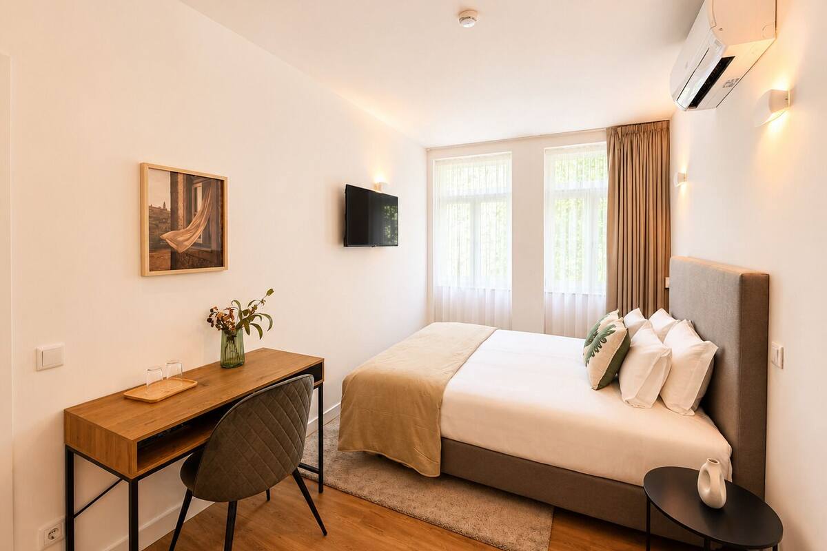 Quarto com cama, escrivaninha, cadeira, televisão e aparelho de ar condicionado.