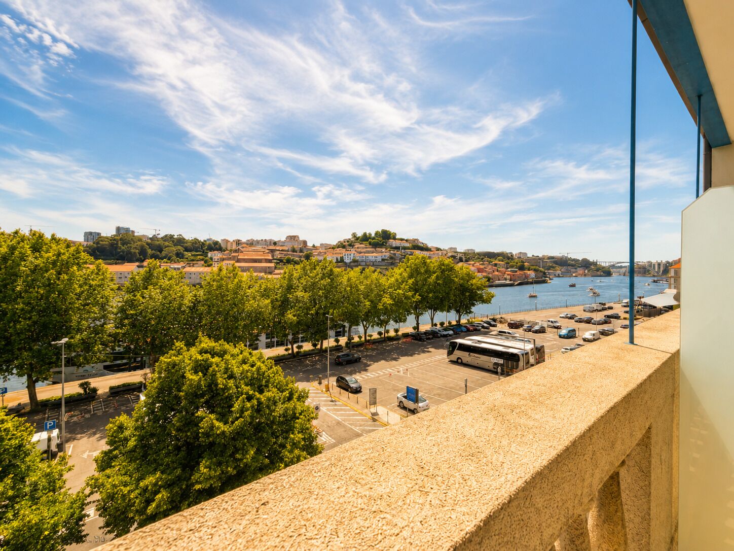 Paisagem costeira com vista para o mar, área de estacionamento e um edifício com varanda a contemplar a cena.