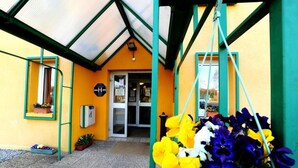 Entrada de edifício com porta de vidro, janela emoldurada em verde e um cesto de flores pendurado.