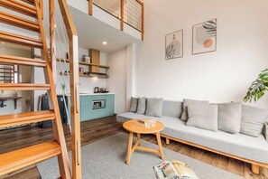 Um espaço de estar moderno com escada, sofá, mesa pequena e área de cozinha.
