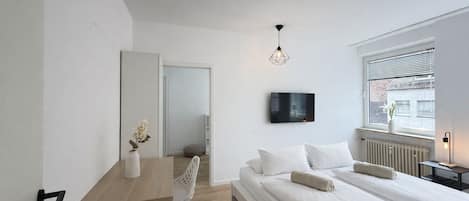 Quarto moderno com cama, mesa de cabeceira, cadeira e televisão fixada na parede.