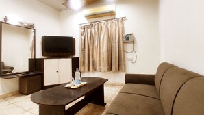 Uma sala de estar com sofá, televisão na parede, uma mesinha e uma janela com cortinas.
