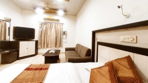 Quarto de hotel com cama, sofá, televisão, escrivaninha e telefone.