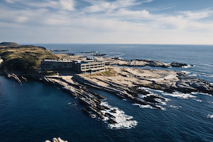 Um hotel à beira-mar com estrutura em vários andares, localizado em terreno rochoso e vista para o mar.