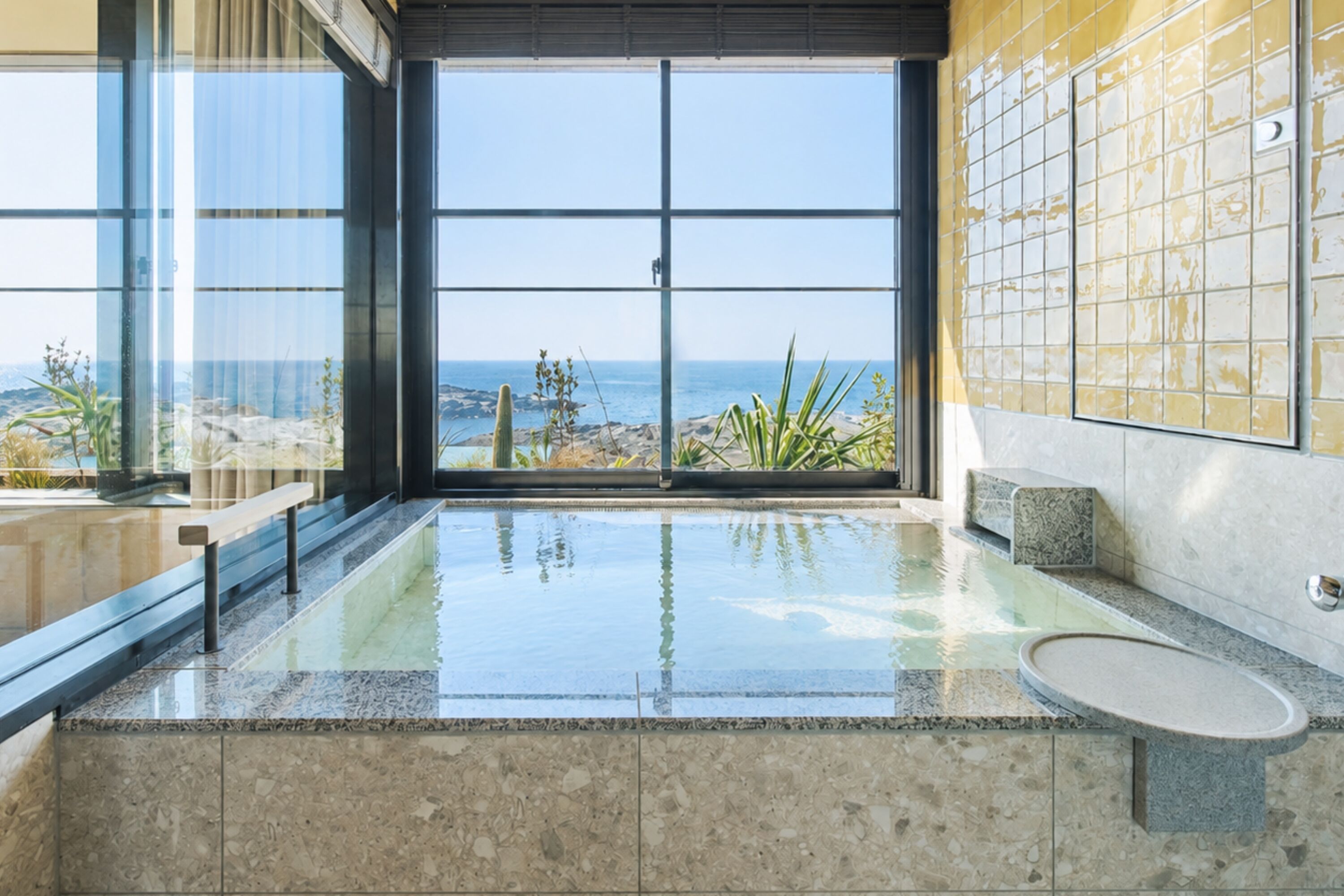 Piscina interior moderna com vista para o mar, apresentando uma parede de vidro e uma parede revestida em azulejos.