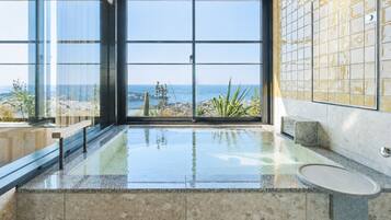 Piscina interior moderna com vista para o mar, apresentando uma parede de vidro e uma parede revestida em azulejos.