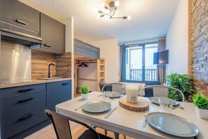 Cozinha moderna com armários cinza, exaustor de aço inoxidável e painel de parede de madeira. Há uma área de jantar com mesa branca posta para dois, incluindo pratos, talheres e uma vela.