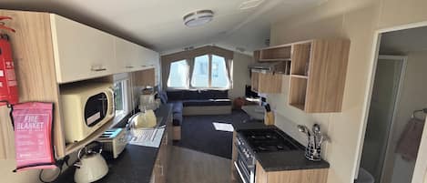 Cozinha compacta com fogão, micro-ondas e pia, armários de madeira e janela que traz luz natural.
