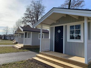 Fileira de pequenas cabanas térreas com fachada branca e portas escuras, cada uma com um pequeno alpendre e degraus que levam à entrada.