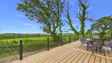 Um deck de madeira com mobiliário de exterior, rodeado por vegetação e uma vista desobstruída para o campo.
