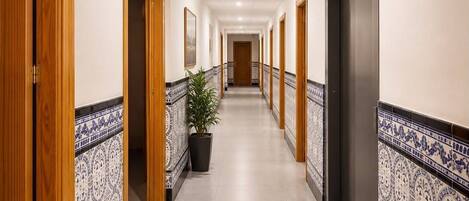 Corredor de hotel com portas de madeira, paredes azulejadas e um vaso de planta.