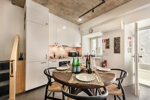 Uma cozinha moderna com armários brancos, uma mesa de jantar posta com pratos, copos e garrafas, e vista para o exterior.
