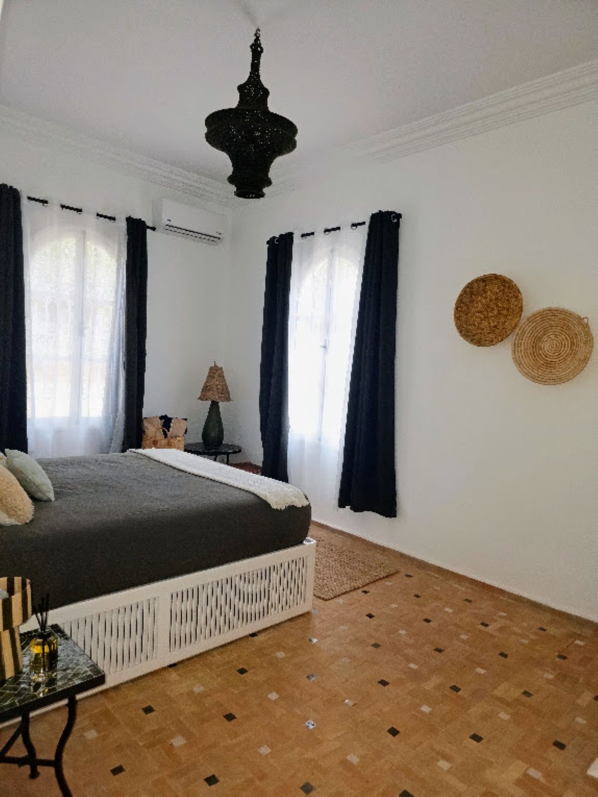 Quarto com cama, mesa de cabeceira, abajur e duas decorações de parede em tear.